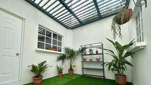 Um pequeno jardim interior com grama artificial, plantas em vasos, uma janela e uma estante de metal.