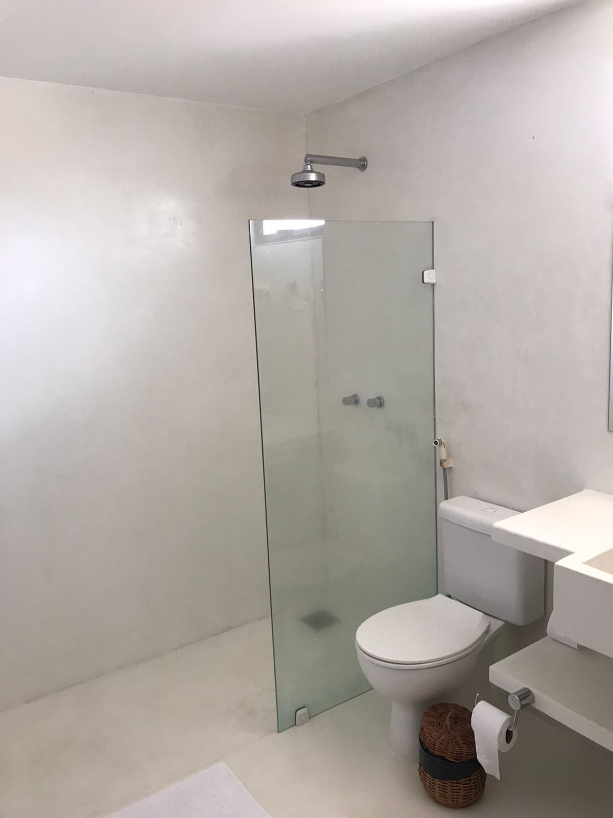 Uma casa de banho moderna com cabine de duche em vidro, sanita branca e lavatório branco com espelho em cima.