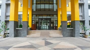 Entrada de hotel com piso de padrão geométrico, grandes portas de vidro e pilares amarelos.