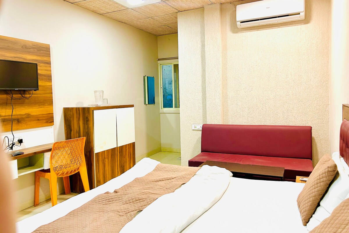 Quarto de hotel com cama, escrivaninha, cadeira, televisão e aparelho de ar condicionado.