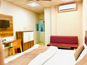Quarto de hotel com cama, escrivaninha, cadeira, televisão e aparelho de ar condicionado.