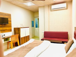 Quarto de hotel com cama, escrivaninha, cadeira, televisão e aparelho de ar condicionado.