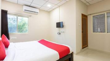 Quarto de hotel com uma cama, televisão fixada na parede e janela com cortinas.