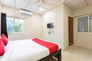 Quarto de hotel com uma cama, televisão fixada na parede e janela com cortinas.