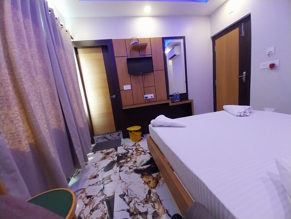 Quarto de hotel com uma cama, televisão na parede, secretária pequena e um cesto de lixo.