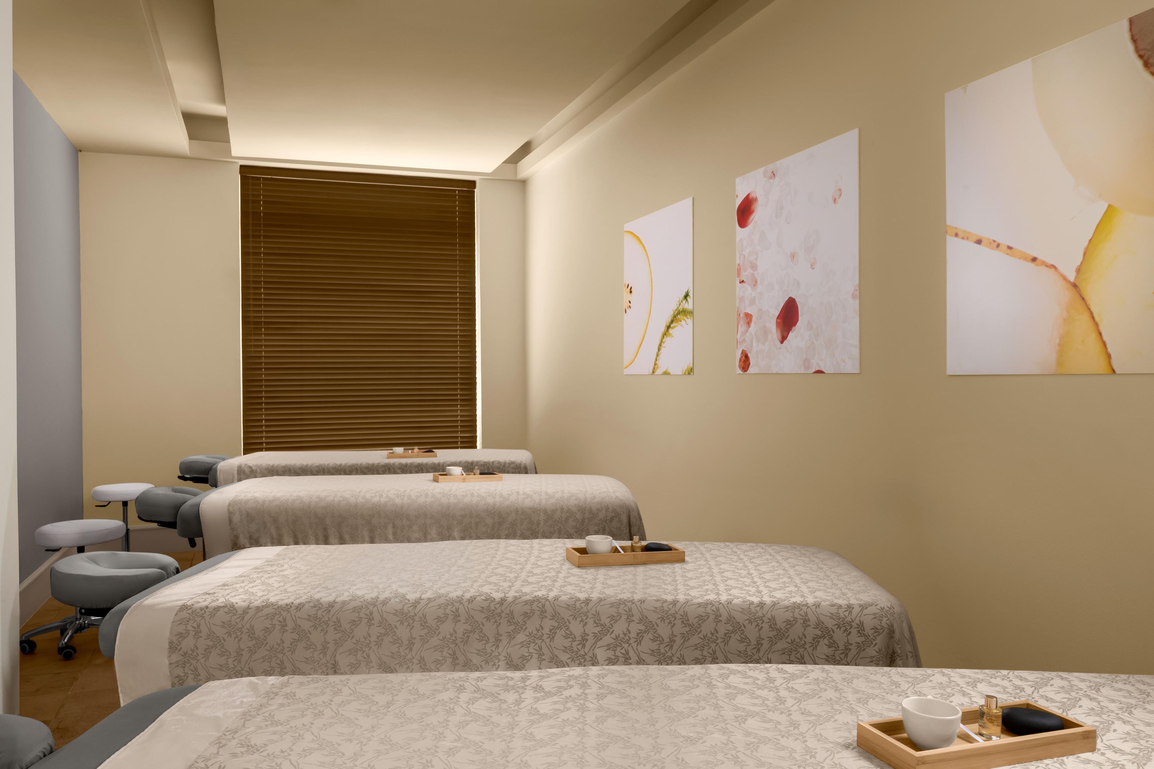 Um espaço de spa com duas camas, uma cadeira de massagem e obras de arte nas paredes.
