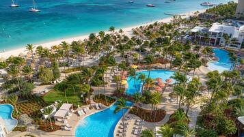 Resort com uma piscina grande, palmeiras e uma praia com barcos.