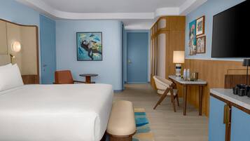 Quarto de hotel com cama, escrivaninha, cadeira, televisão e obras de arte nas paredes.