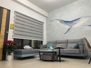 Uma sala de estar moderna com um sofá cinzento, uma mesa de centro e um grande mural de uma baleia.