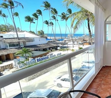 Varanda com vista para uma praia, palmeiras e um letreiro que diz 'blanca beach club'.