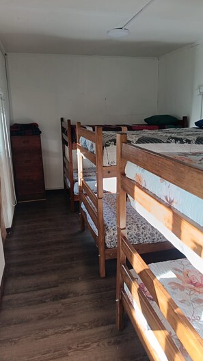 Quarto de estudante com beliches, cômoda de madeira e janela.