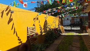 Paredes amarelas com uma escada de madeira e plantas em vasos. Bandeiras estão penduradas acima.