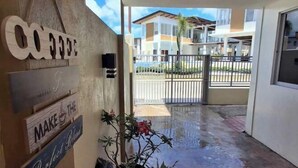 Entrada de hotel com uma placa de madeira, um vaso de planta e vista dos edifícios ao redor.