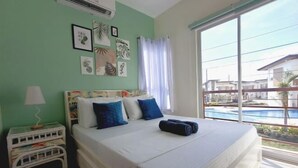 Quarto com cama, mesa de cabeceira, abajur e vista para uma piscina.
