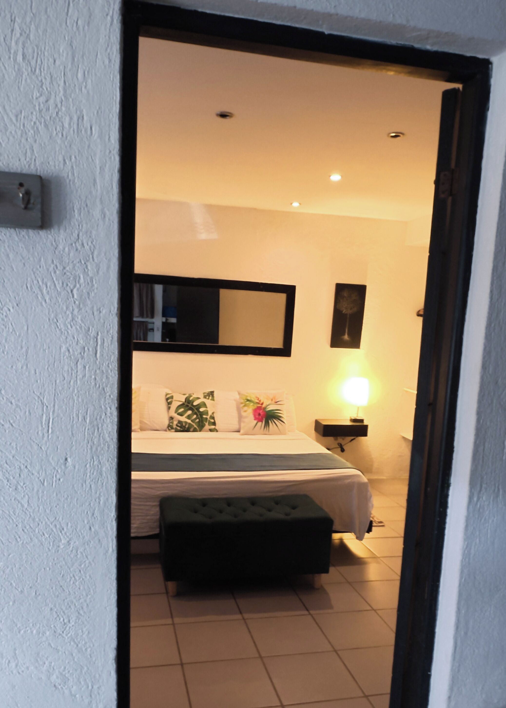 Quarto com uma cama, mesa de cabeceira, abajur e espelho na parede.