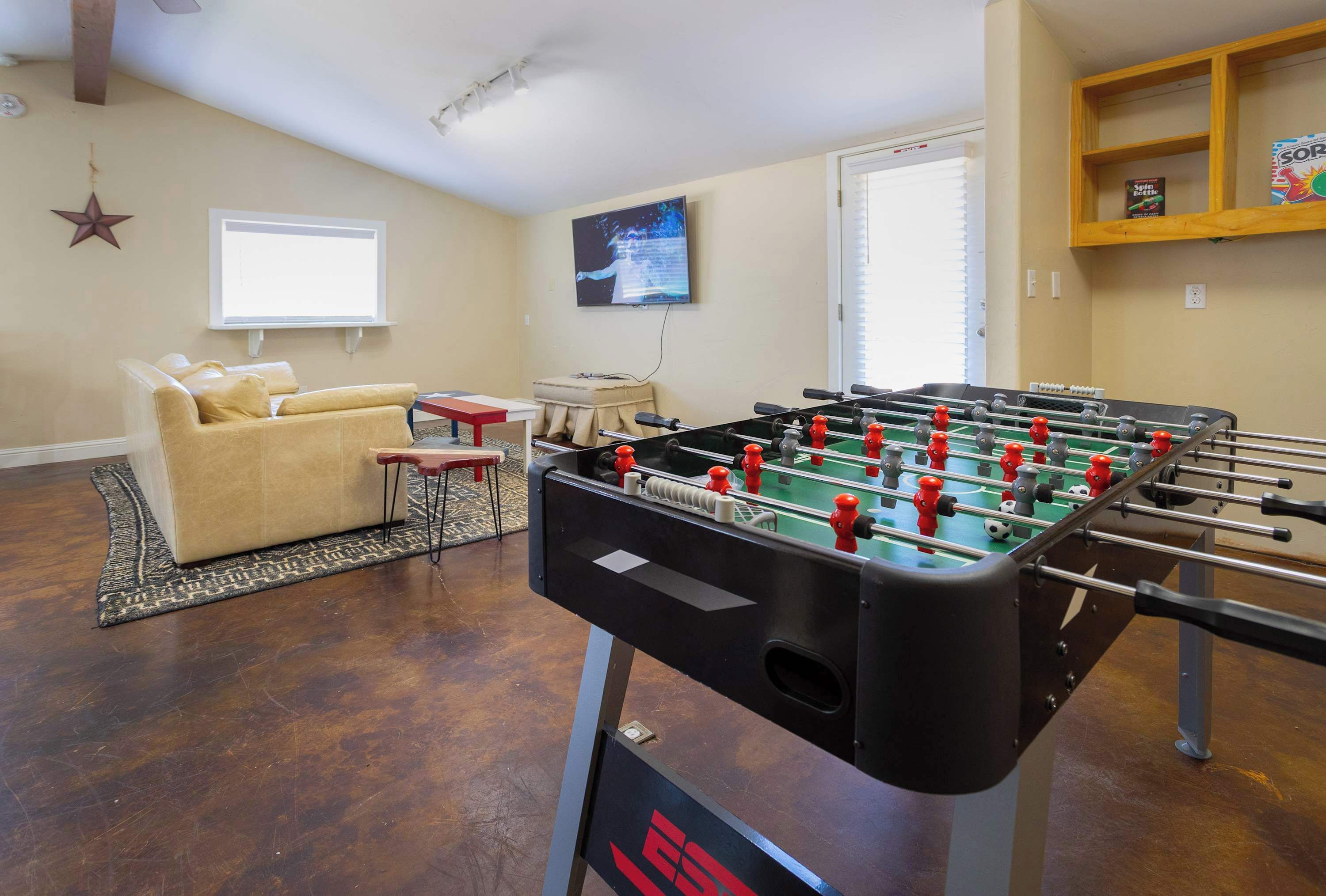 Uma sala de estar com mesa de futebol, sofá, televisão e um adorno em formato de estrela na parede.