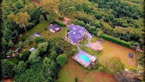 Vista aérea de uma propriedade com piscina, duas casas e densa mata ao redor.