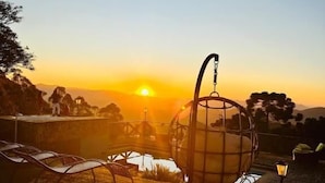 Vista do pôr do sol com uma cadeira pendurada esférica e espreguiçadeiras em um jardim.