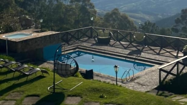 Uma área de piscina com vista para montanhas distantes, rodeada por um terraço com cadeiras e uma banheira de hidromassagem.