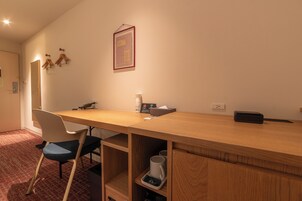 Quarto de hotel com escrivaninha de madeira, uma cadeira, máquina de café e um aviso emoldurado na parede.