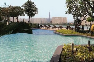 Piscina com espreguiçadeiras, cercada por vegetação e um horizonte urbano ao fundo.