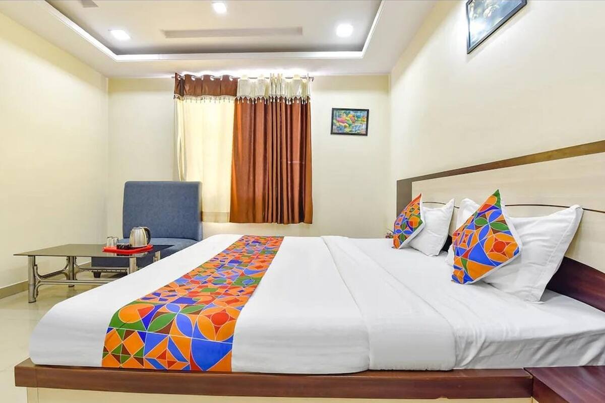 Quarto de hotel com cama, uma mesinha com bandeja, uma cadeira e janela com cortinas.