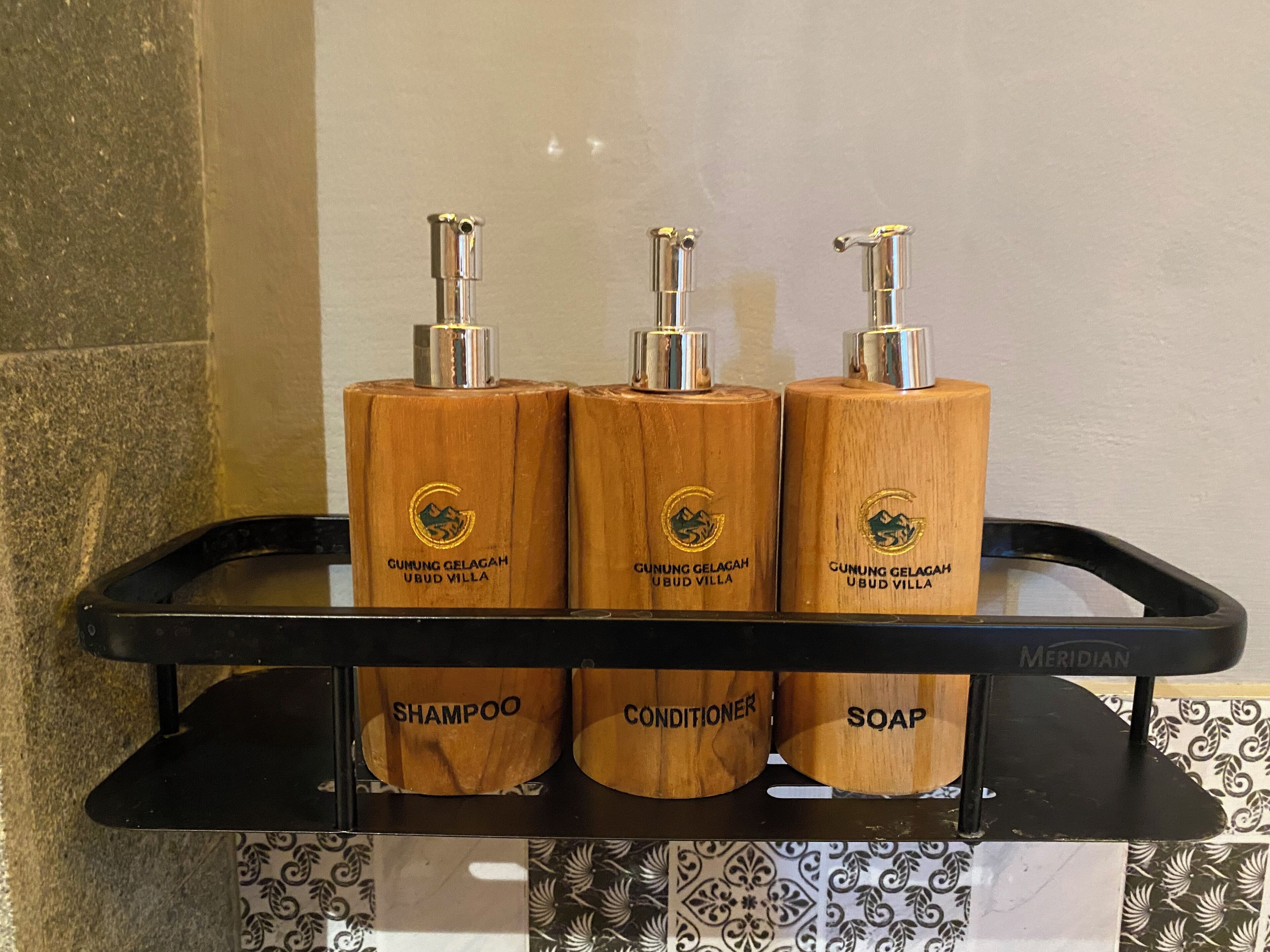 Três garrafas de madeira com shampoo, condicionador e sabonete sobre um suporte preto.