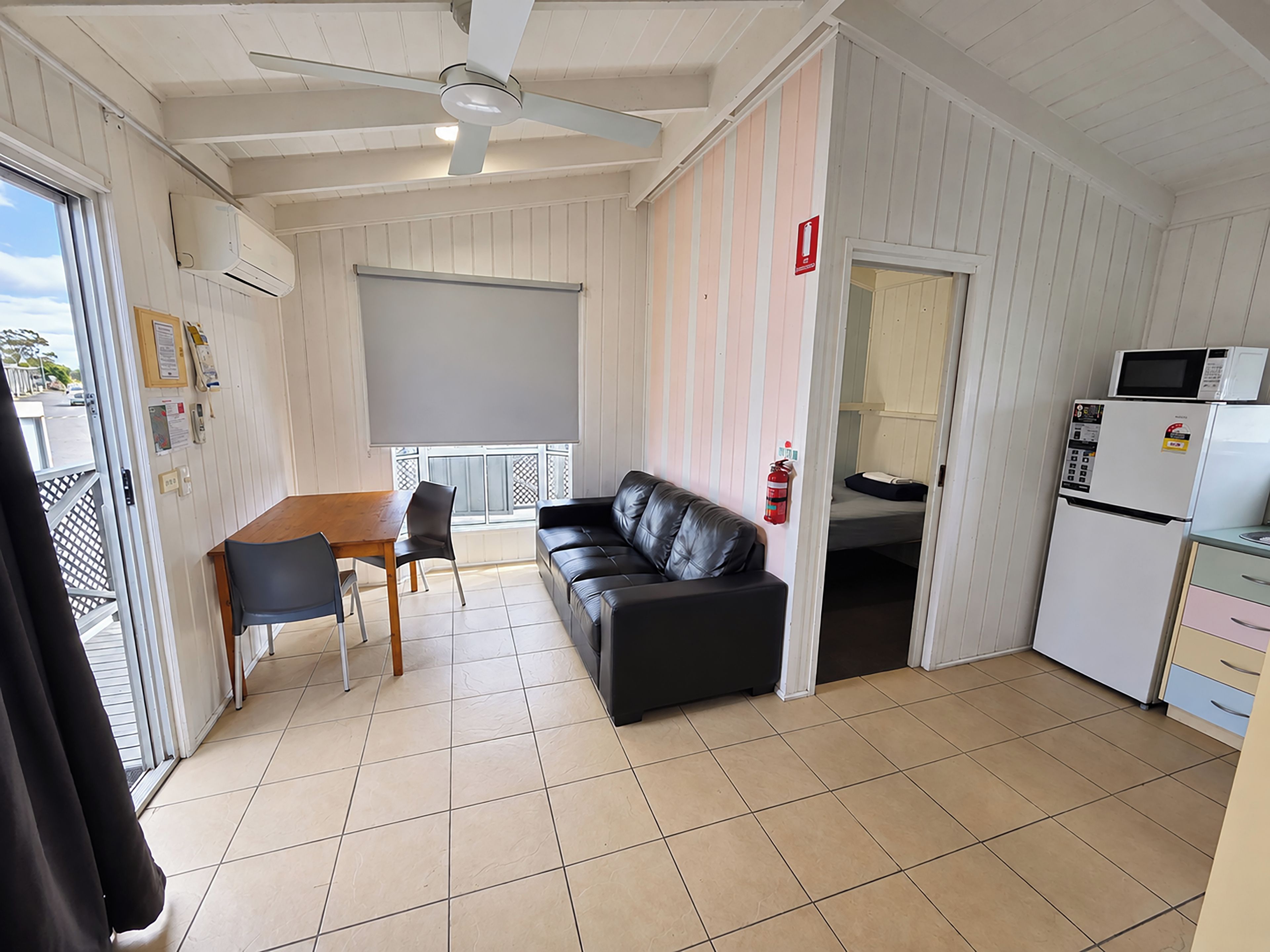 Quarto com mesa de jantar, cadeiras, sofá, ventilador de teto, cozinha compacta com micro-ondas e extintor de incêndio.