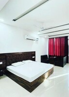 Quarto de hotel moderno com cama grande, televisão de tela plana e área de estar com cortinas vermelhas.