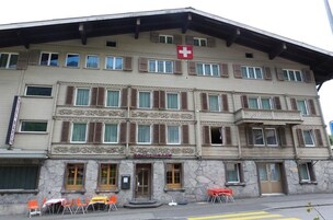 Um edifício de vários andares com uma bandeira suíça, um letreiro de restaurante e área externa com mesas e cadeiras.