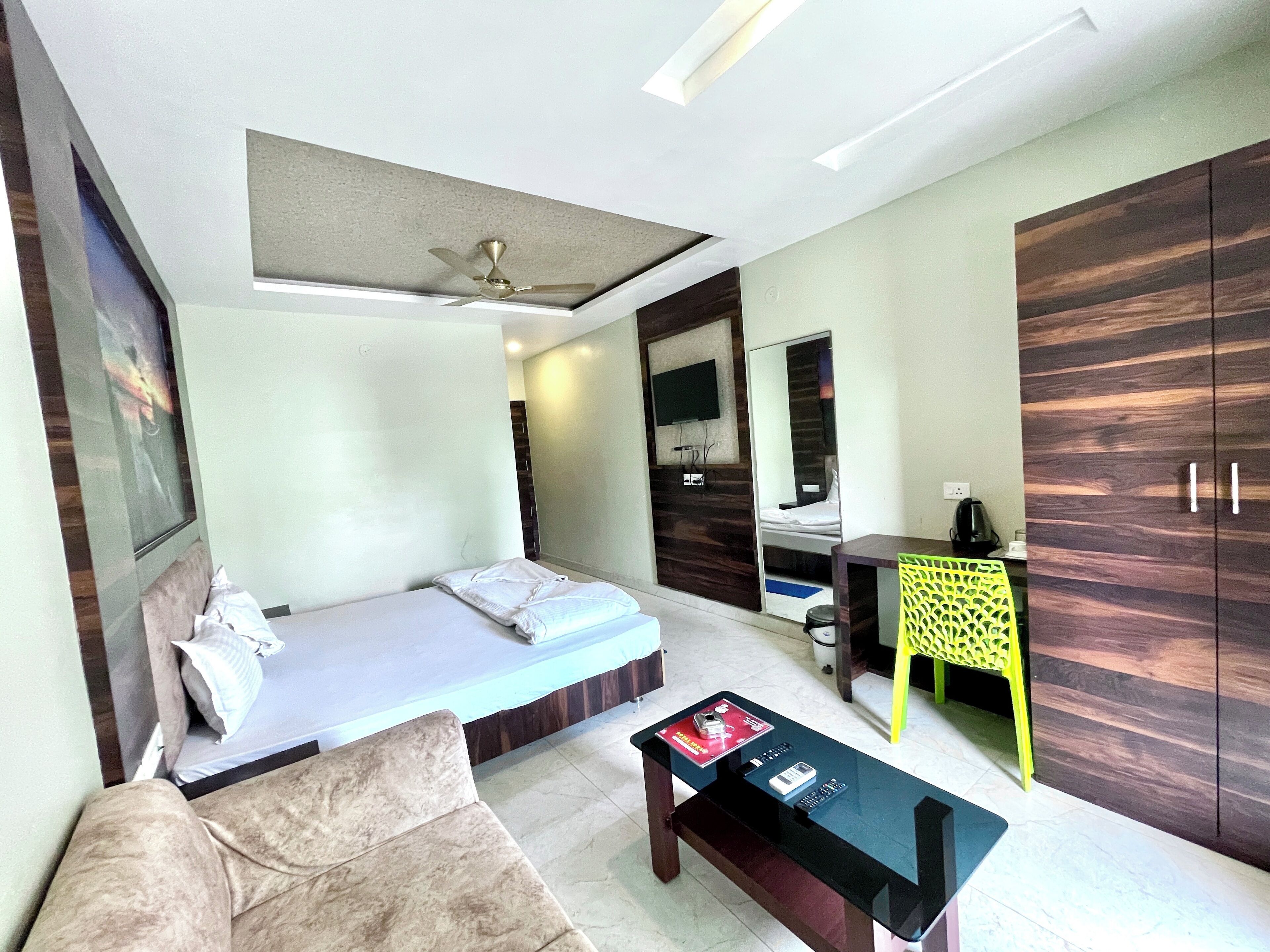 Quarto de hotel moderno com cama, sofá, escrivaninha, espelho e guarda-roupa.