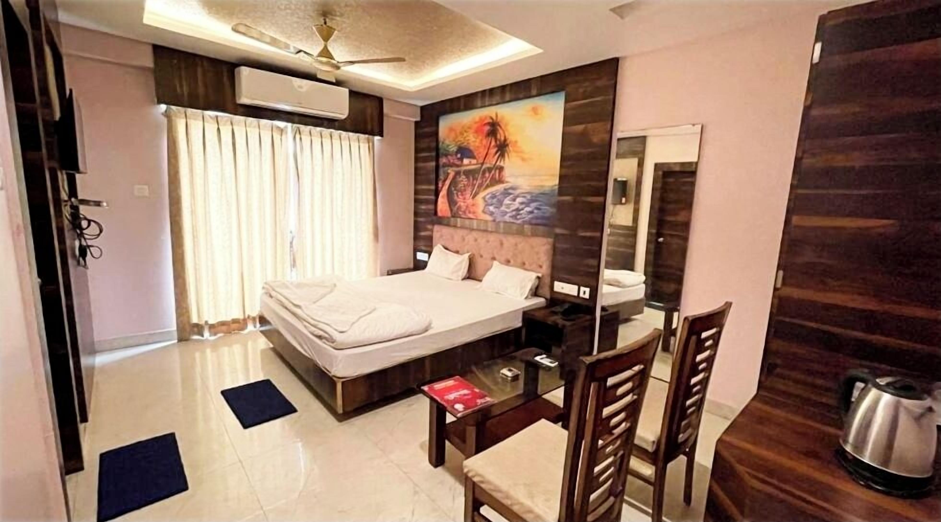 Quarto de hotel com cama, escrivaninha, cadeira, cafeteira e um quadro na parede.