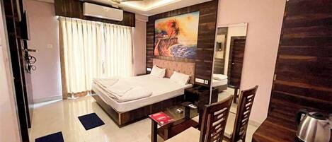 Quarto de hotel com cama, escrivaninha, cadeira, cafeteira e um quadro na parede.
