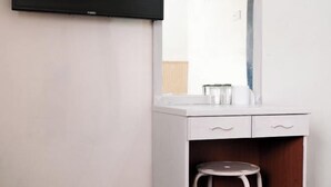 Uma toucador branca com espelho, um banquinho pequeno e uma televisão de tela plana fixada na parede.