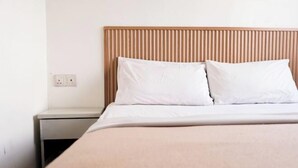 Uma cama com cabeceira de madeira, roupa de cama branca e mesa de cabeceira com tomada.