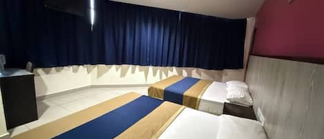 Quarto de hotel com duas camas, uma escrivaninha, uma televisão e uma cortina.
