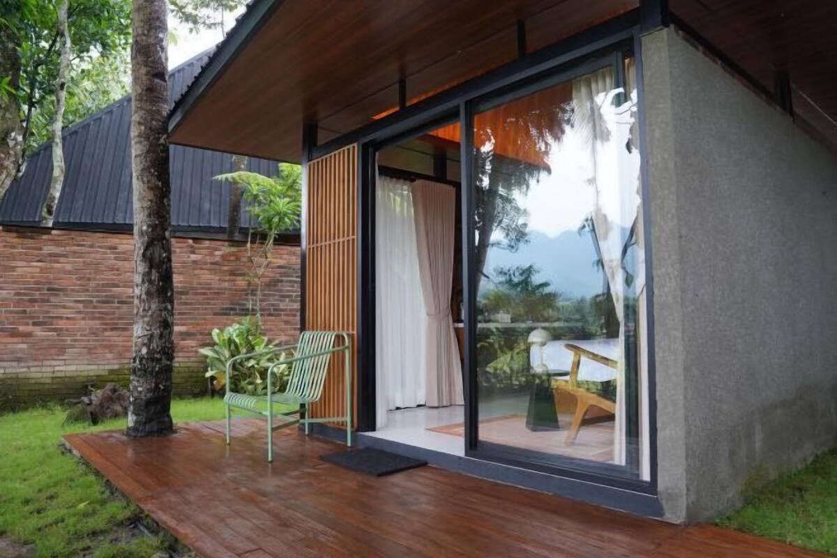 Uma casa moderna com deck de madeira, uma cadeira verde e porta de vidro que dá para um espaço de pátio.