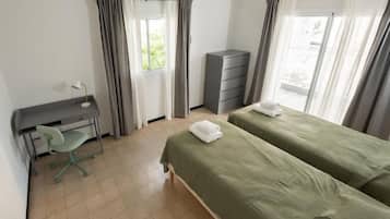 Quarto com duas camas, uma escrivaninha, uma cadeira, uma cômoda e uma janela com cortinas.