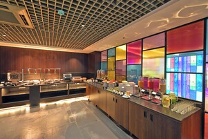 Cozinha moderna com bancada comprida, diversos eletrodomésticos e uma janela com decoração colorida.