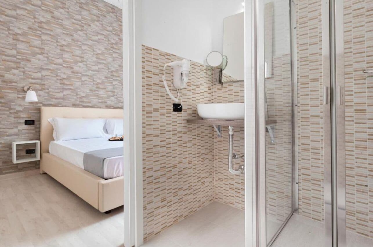 Quarto moderno com cama, mesa de cabeceira e banheiro completo com chuveiro, pia e espelho.