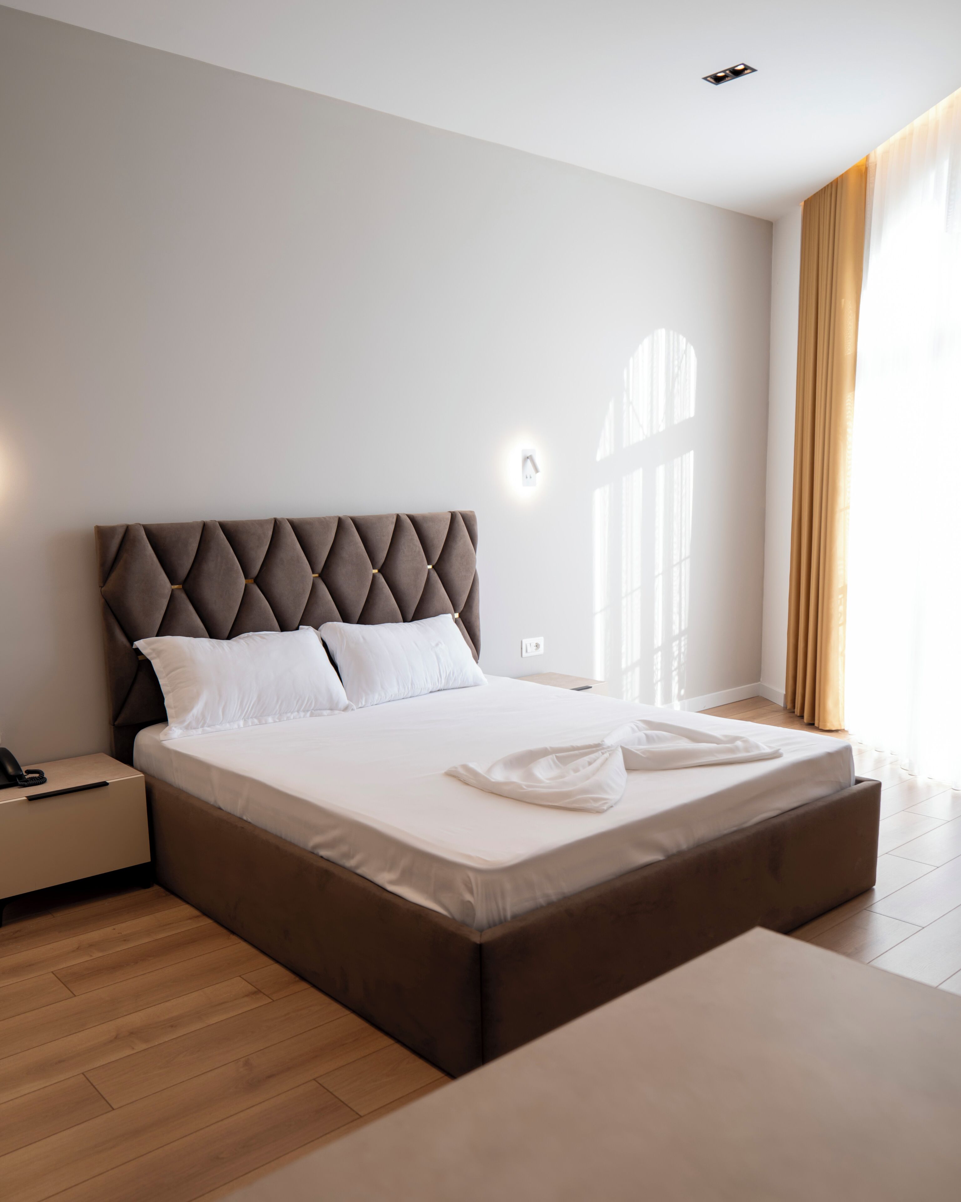 Quarto de hotel moderno com uma cama grande, uma mesinha de cabeceira e um criado-mudo.