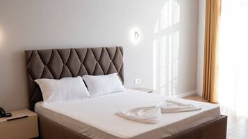 Quarto de hotel moderno com uma cama grande, uma mesinha de cabeceira e um criado-mudo.