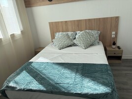 Cama bem arrumada com almofadas estampadas, cabeceira de madeira e mesa de cabeceira com um controle remoto e uma pequena planta.