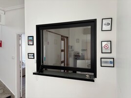 Uma área de recepção com uma janela emoldurada a preto, um sinal de Wi-Fi fixado na parede e vários avisos emoldurados, incluindo um sinal de proibido fumar e um aviso de câmeras de vigilância.