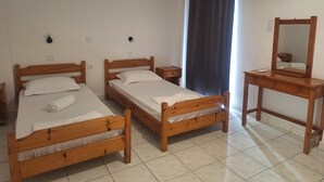 Quarto com duas camas de madeira, uma mesinha de madeira, um espelho e uma cortina escura.