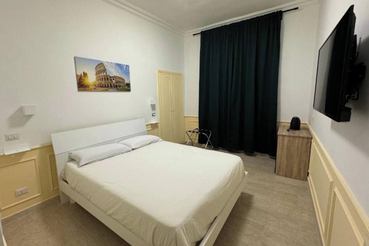 Quarto de hotel com uma cama de solteiro, televisão de tela plana, pintura do Coliseu e cortina escura.