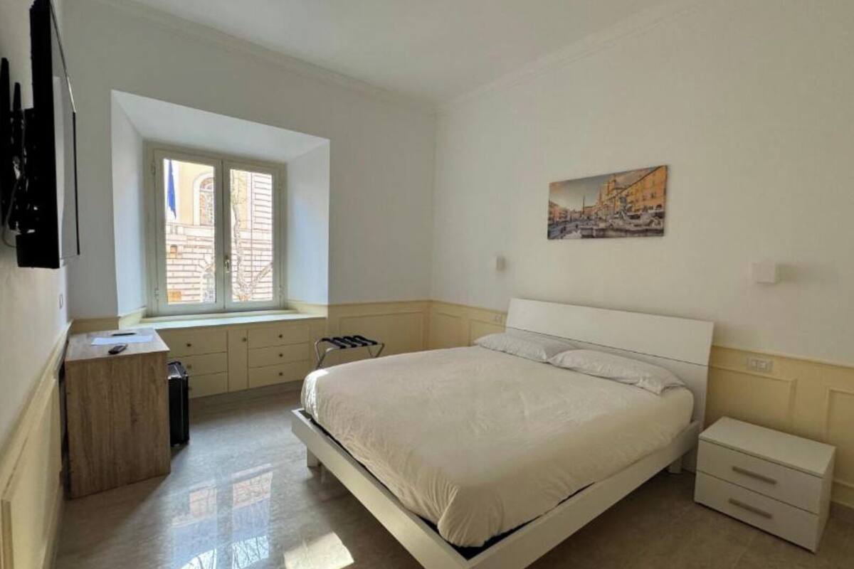 Quarto com cama, escrivaninha, janela e um quadro na parede.