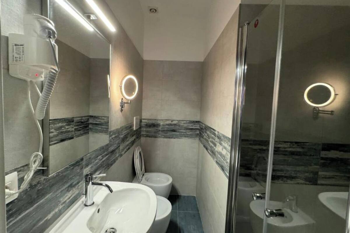 Uma casa de banho moderna com um espelho grande, um secador de cabelo, uma sanita e uma área de duche.
