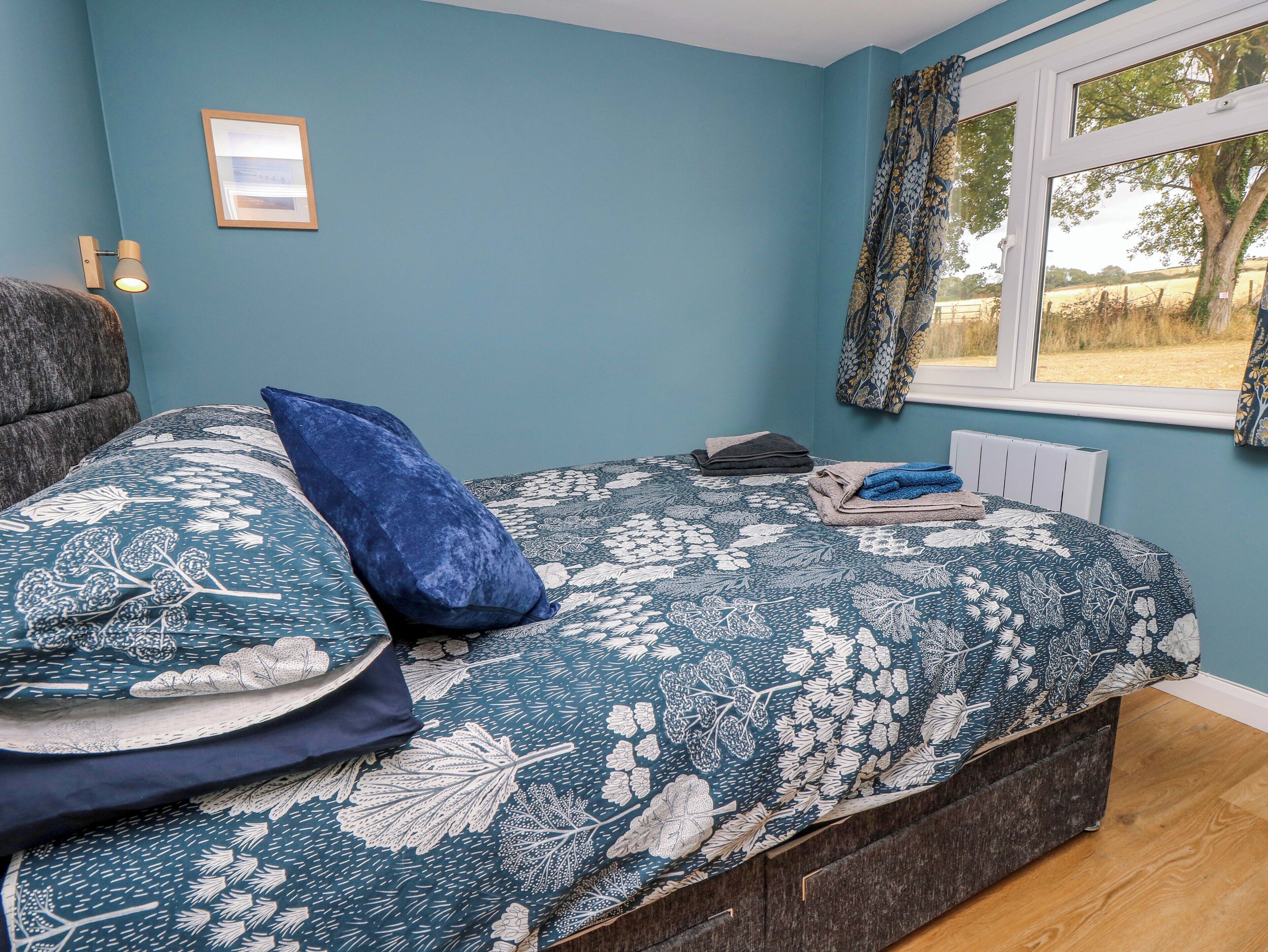 Um quarto com cama, janela com cortinas, radiador e um quadro na parede.
