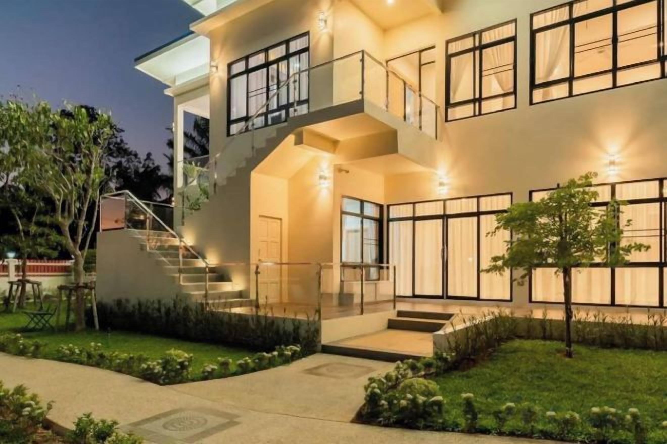 Uma casa de dois andares com varanda, escadaria e entrada bem iluminada.
